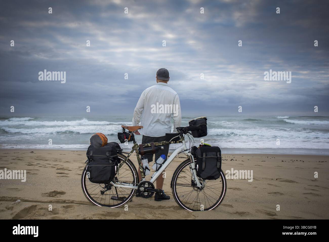 A long distance adventure cyclist stand on a beach in front of his ...