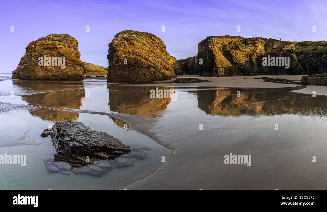 A peaceful sunset on a sandy beach with tidal pools and jagged broken ...