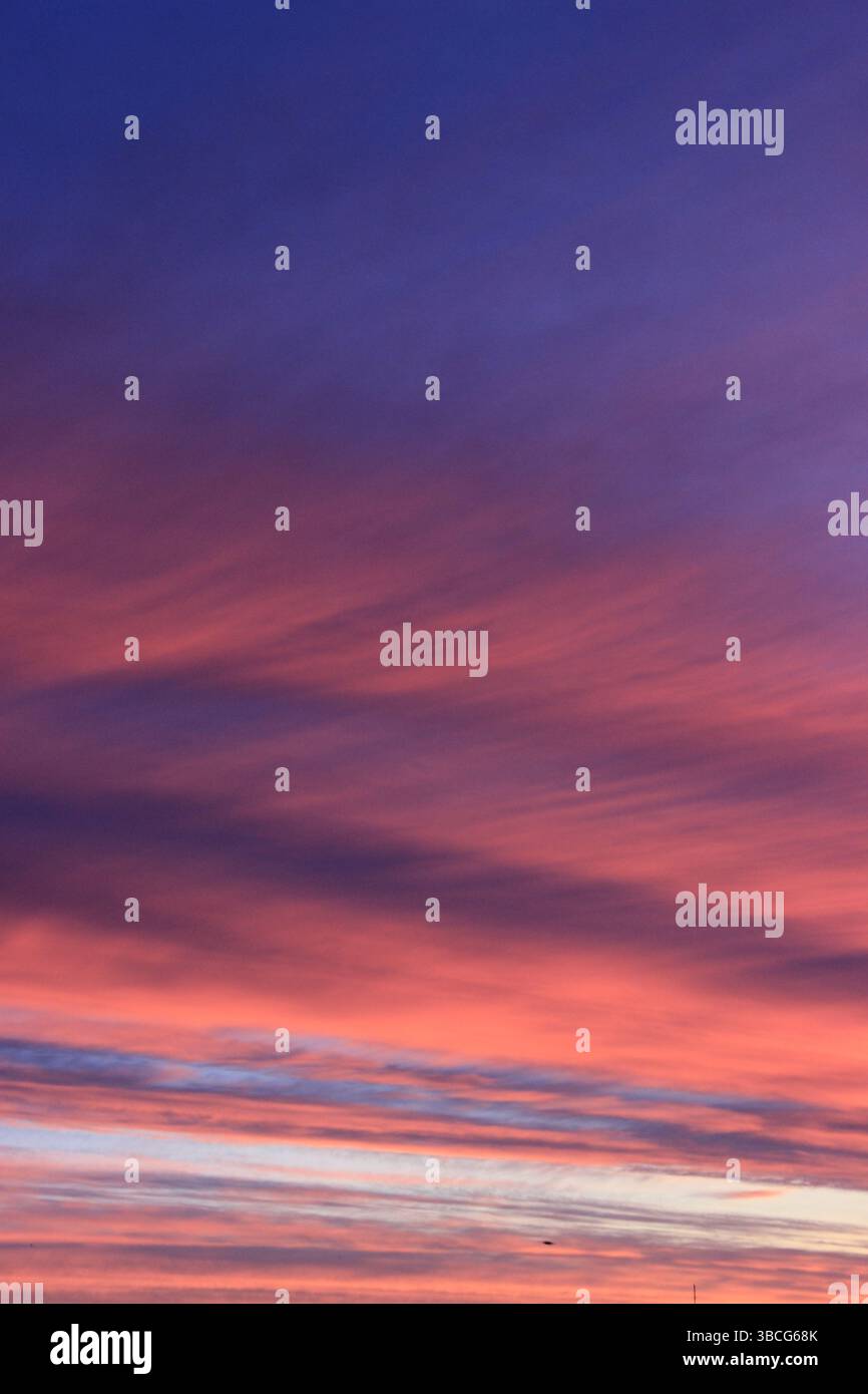 Layered crimson and violet clouds stretch across a twilight sky ...