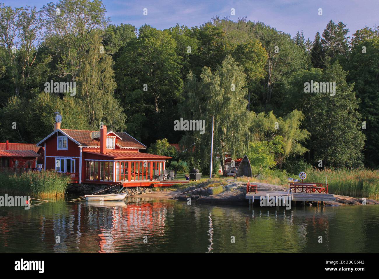 Traditional red Swedish summer cottage with lakeside dock and rowing ...