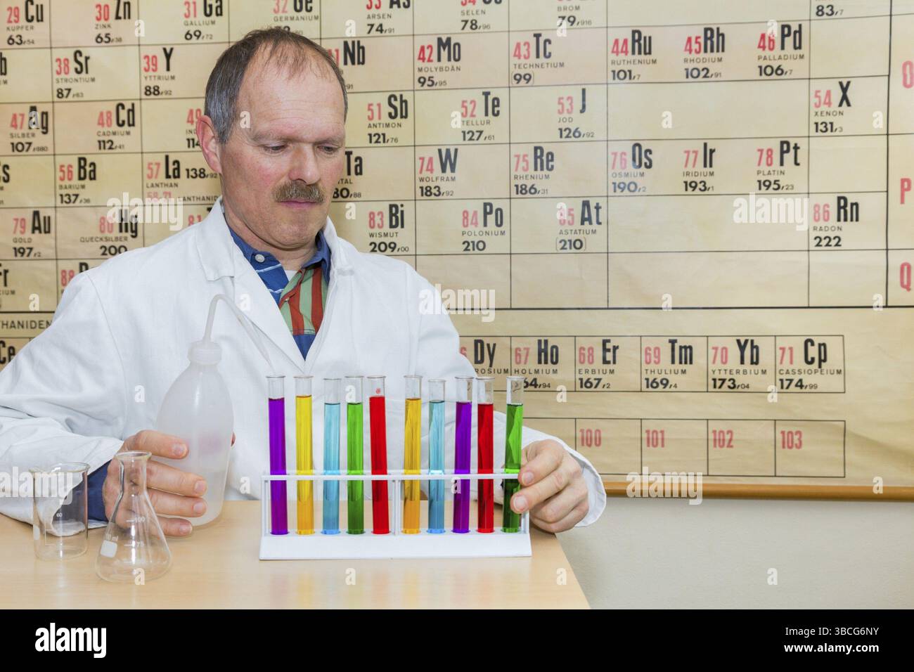 Chemist filling glass tubes with colored liquids in front of wallchart ...