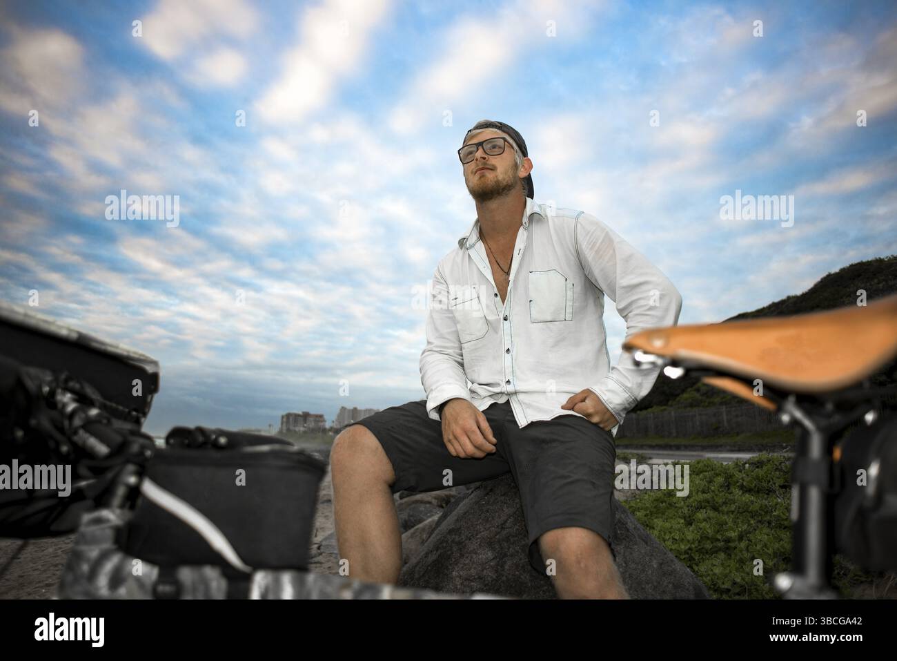A long distance cycle packer sits on a rock near the ocean with his ...