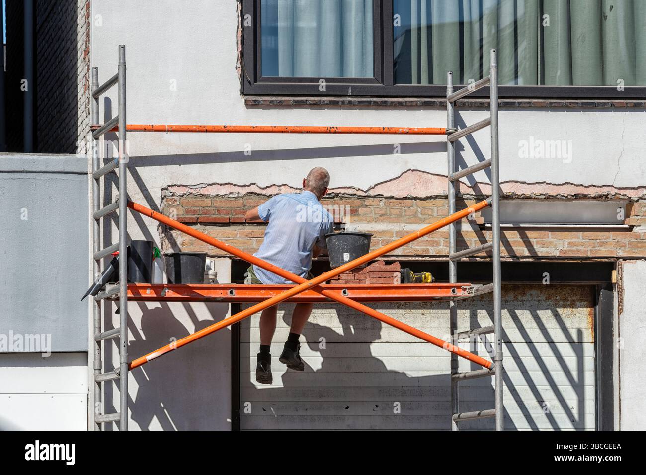 construction worker sits outside on a scaffolding and is busy placing ...