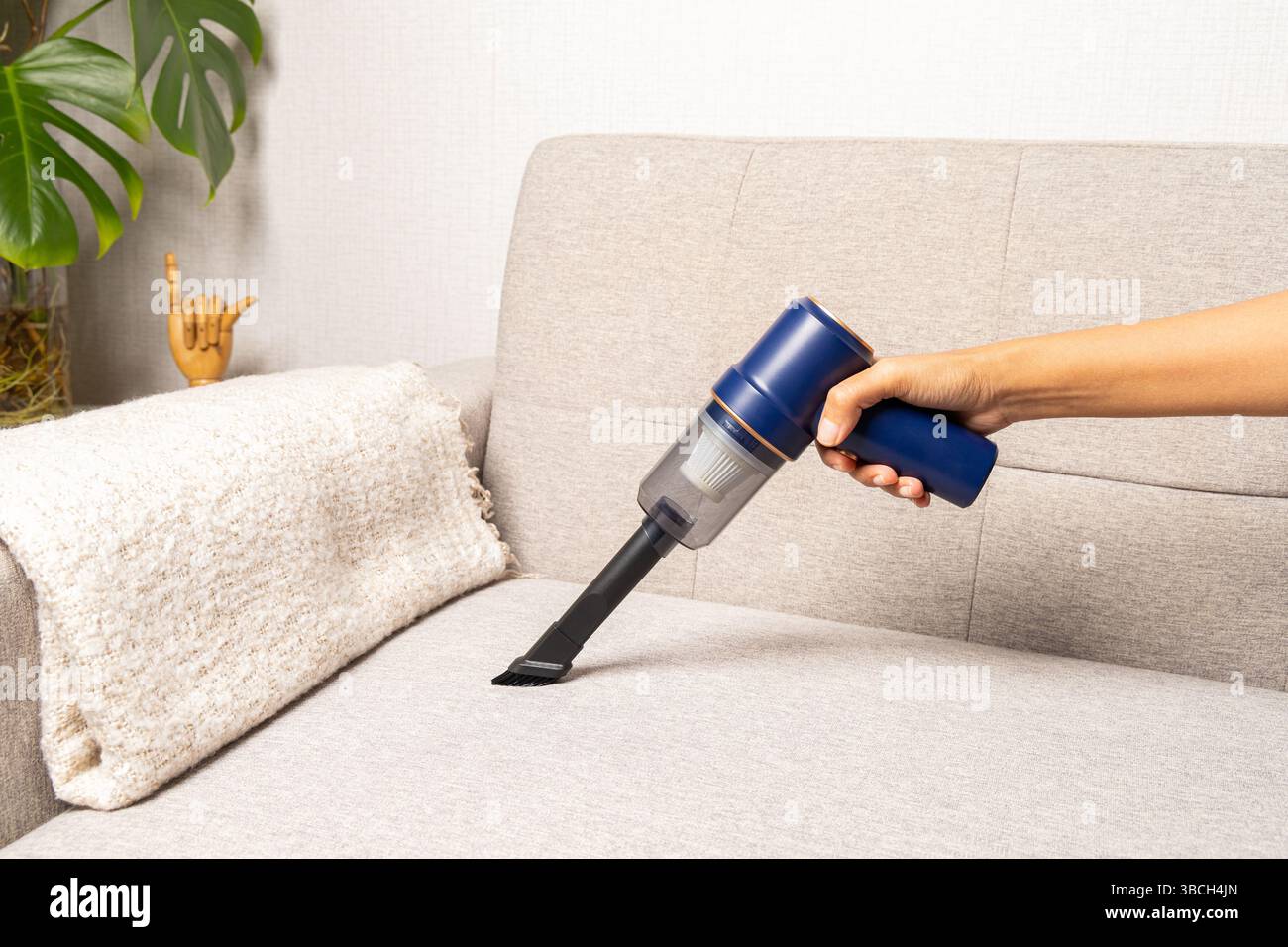 A person is using a vacuum cleaner on a couch. The couch is covered in ...