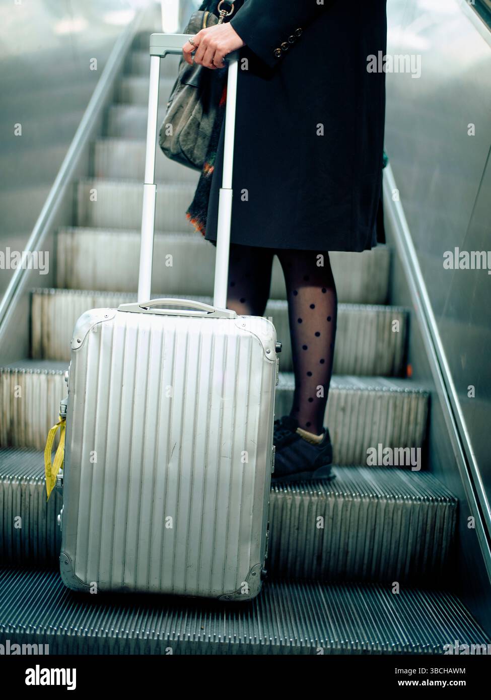 Woman on escalator with spotted tights and silver suitcase, only lower ...