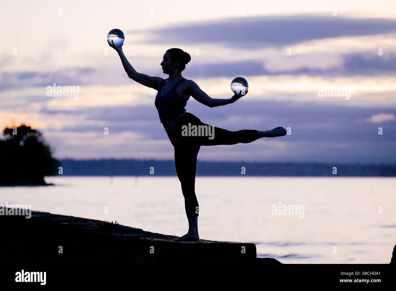 Woman balancing on one leg at sunset holding two reflective spheres. WA ...