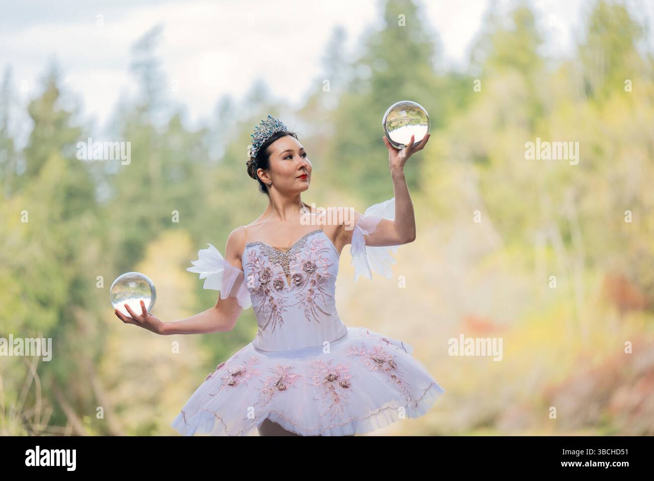 Ballerina wearing a tiara performs with crystal balls in a forest ...