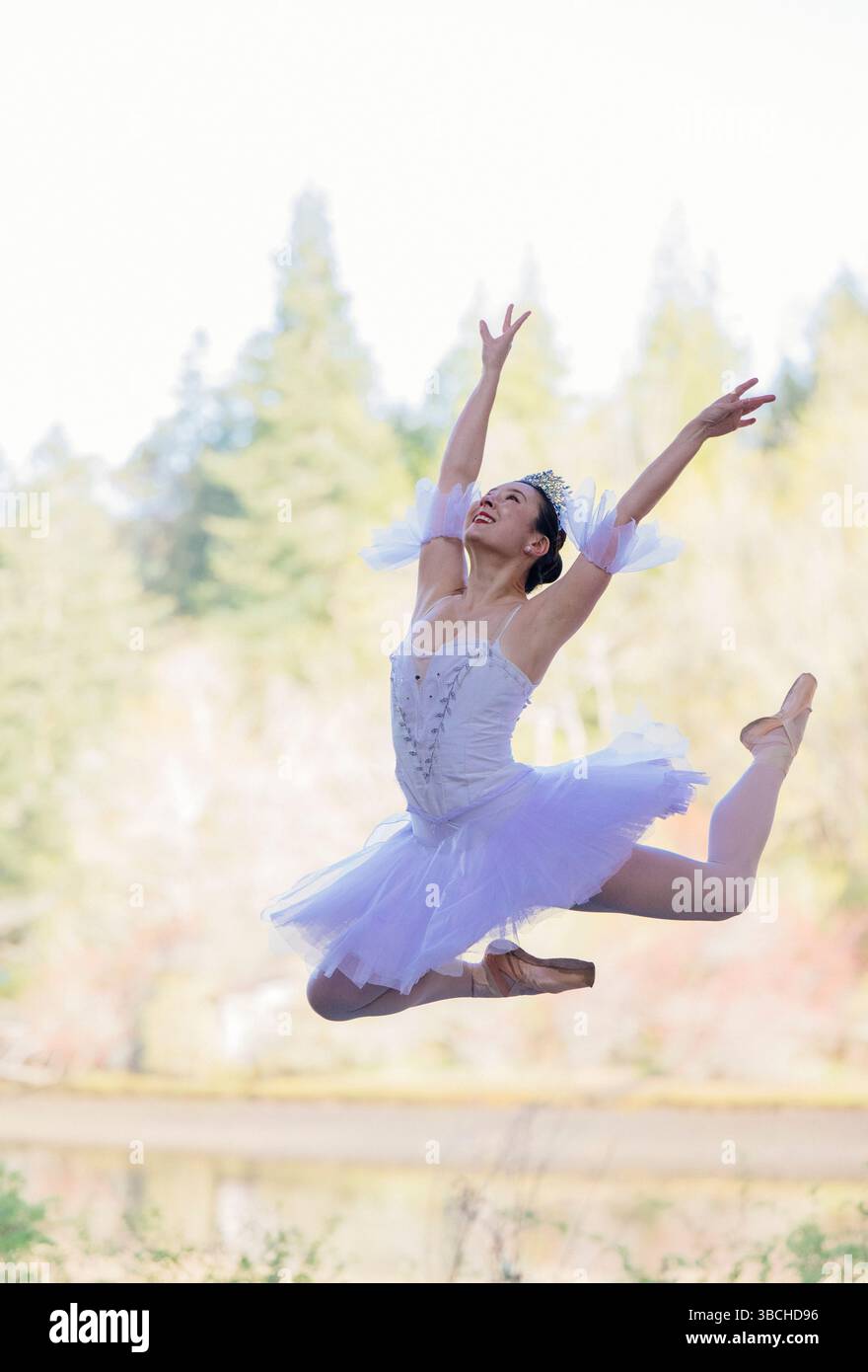 Ballet dancer in mid-air leap against a blurred forest background. WA ...
