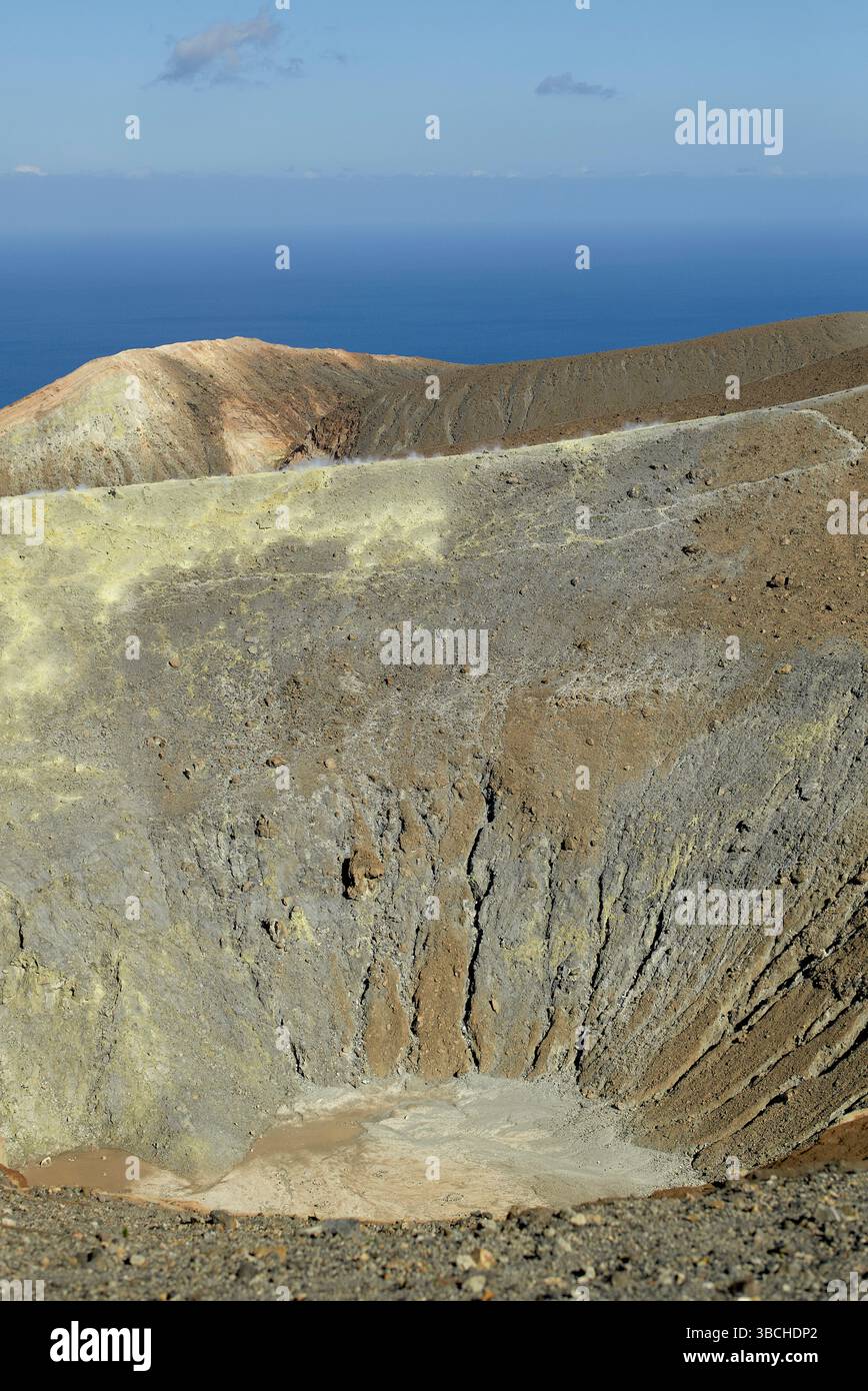 Steaming volcanic crater with rugged terrain and cloudy sky above ...