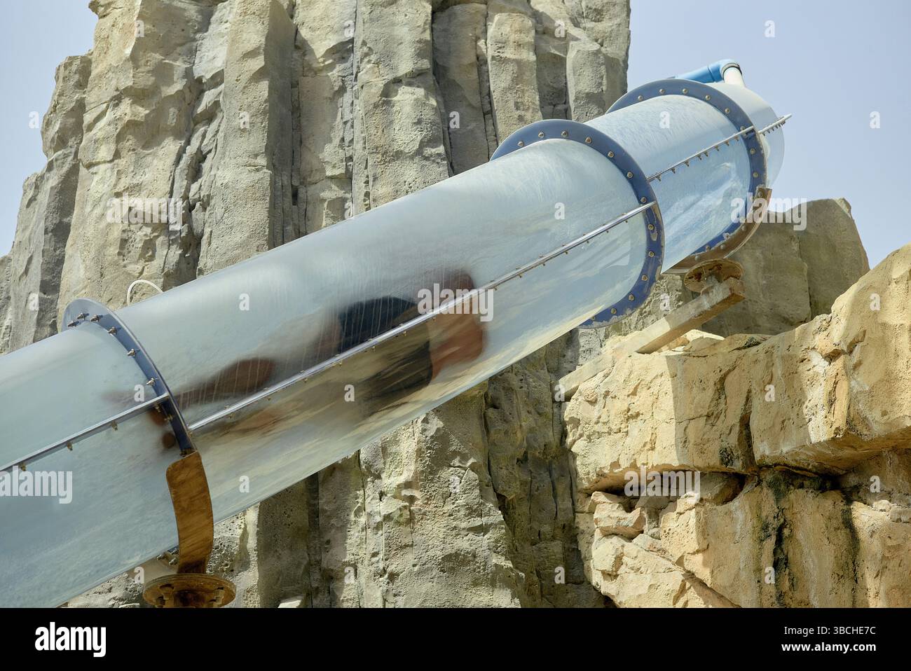 Person sliding through a clear tube slide set against rugged rocky ...