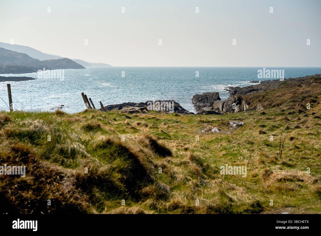 Coastal landscape with grassy hills, rocky shoreline, and calm blue sea ...