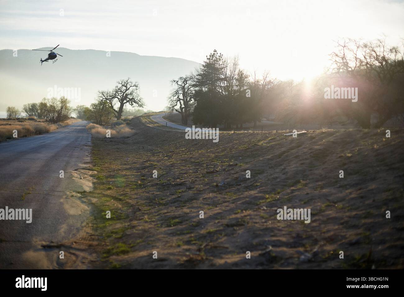 A helicopter flies over a winding road through a barren, sunlit ...