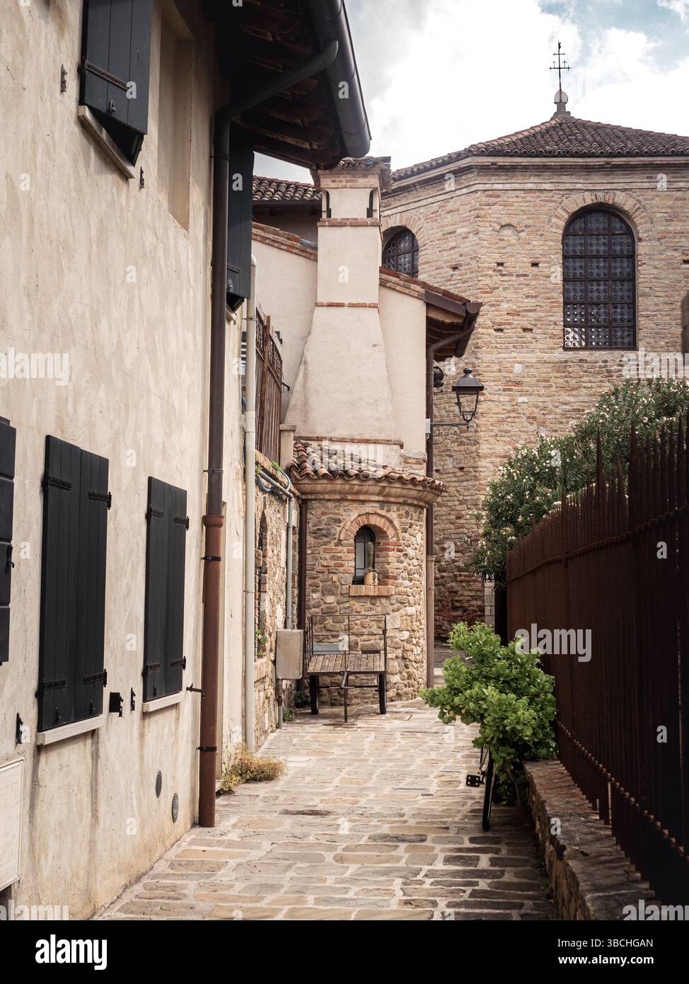 A charming stone alleyway leads past rustic walls and greenery toward ...