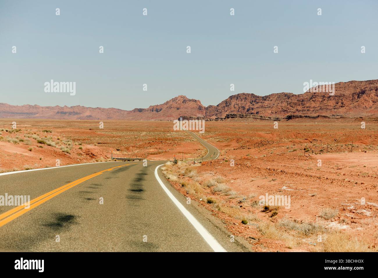 Long winding road through a vast red desert landscape under a clear ...