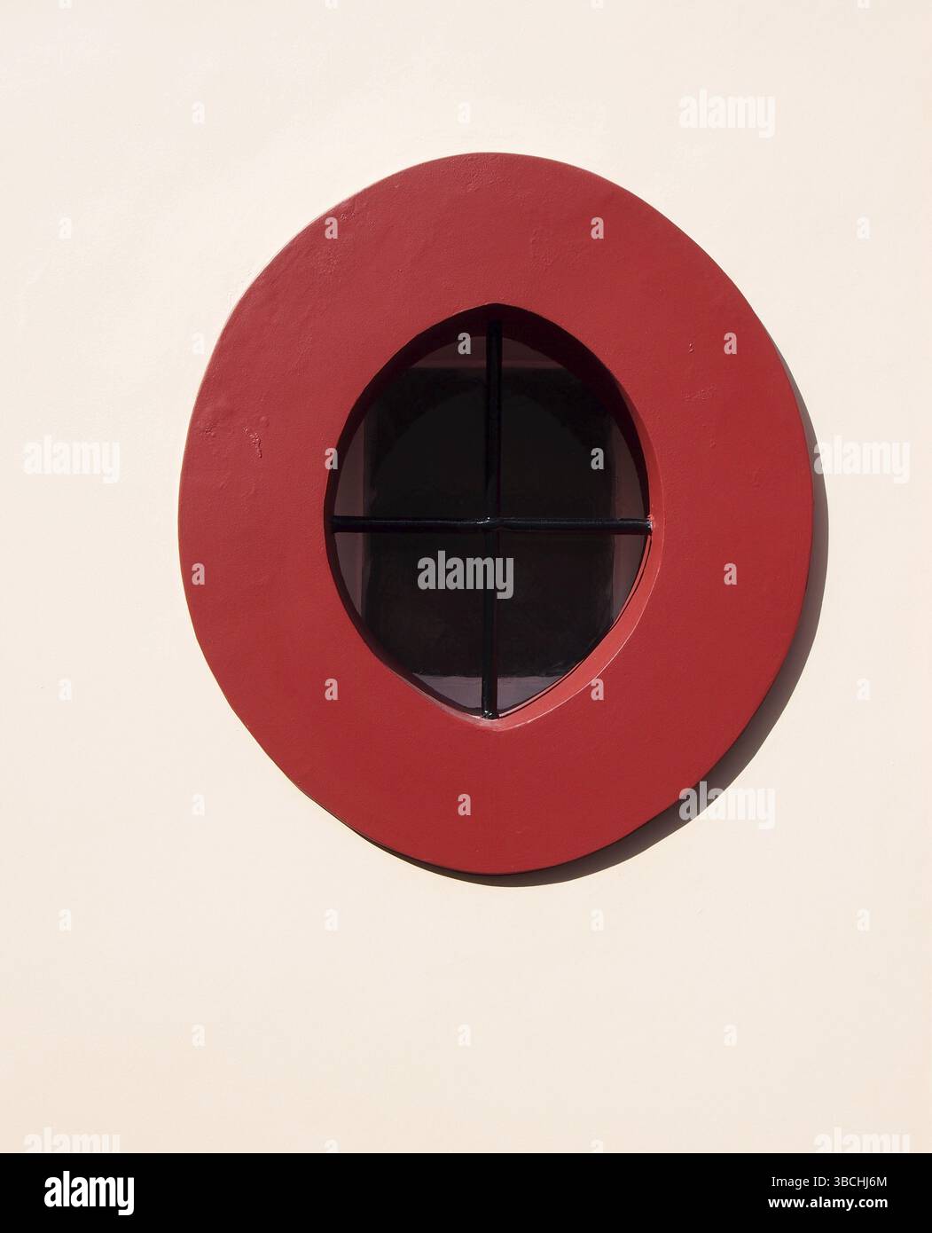 Bright red stone oval window frame in a white wall with black metal ...