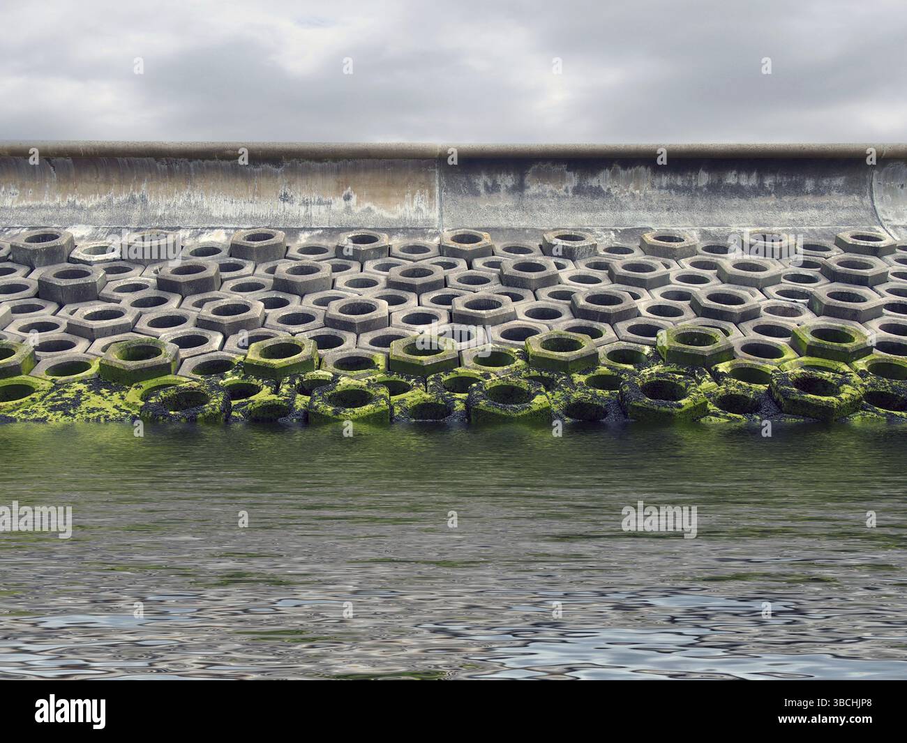 Straight grey concrete defensive sea wall from the sea showing seaweed ...