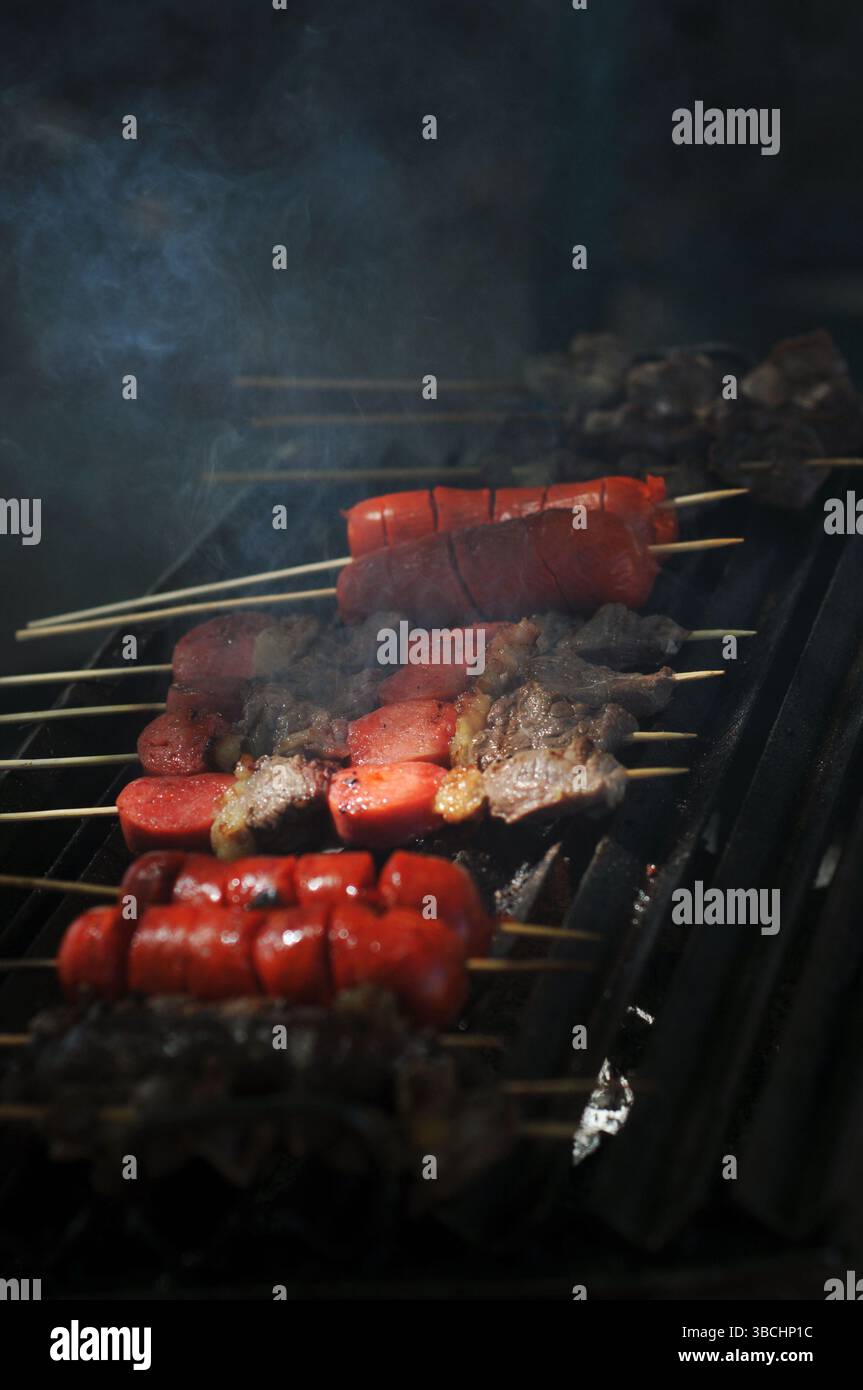 Close-up of skewers with grilled meat and sausages cooking on a ...