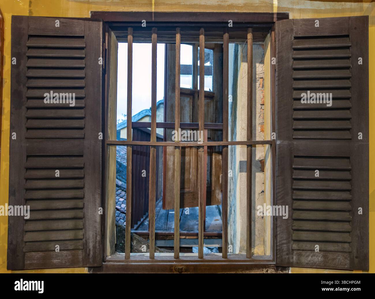 Rustic wooden shutters with bars framing an old window, offering a view ...