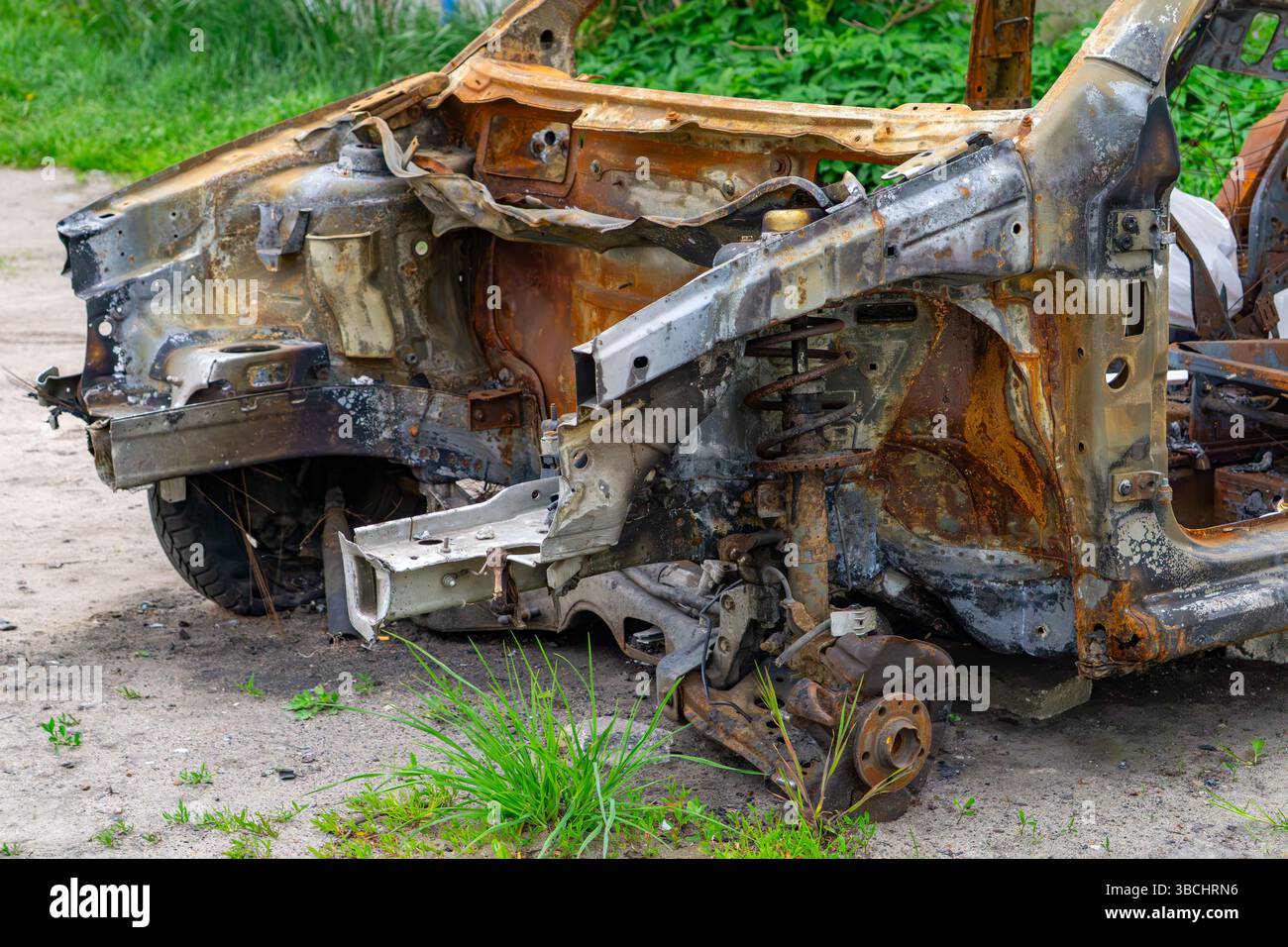 Burnt and partially dismantled car wreck on the roadside. Visible signs ...