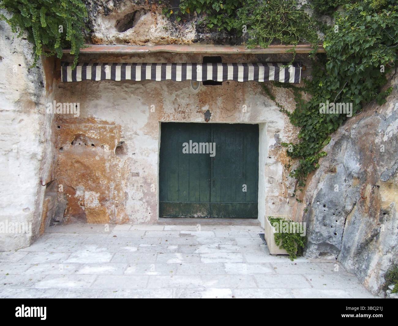 A stone shelter carved out of a cliff with green vegetation wooden ...