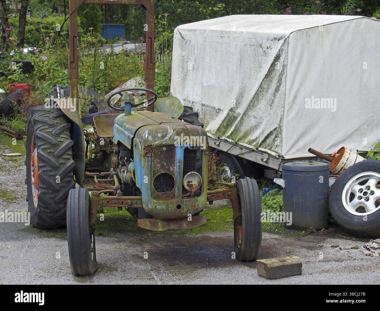 An old rusting abandoned tractor next to a dirty tarpaulin covered ...