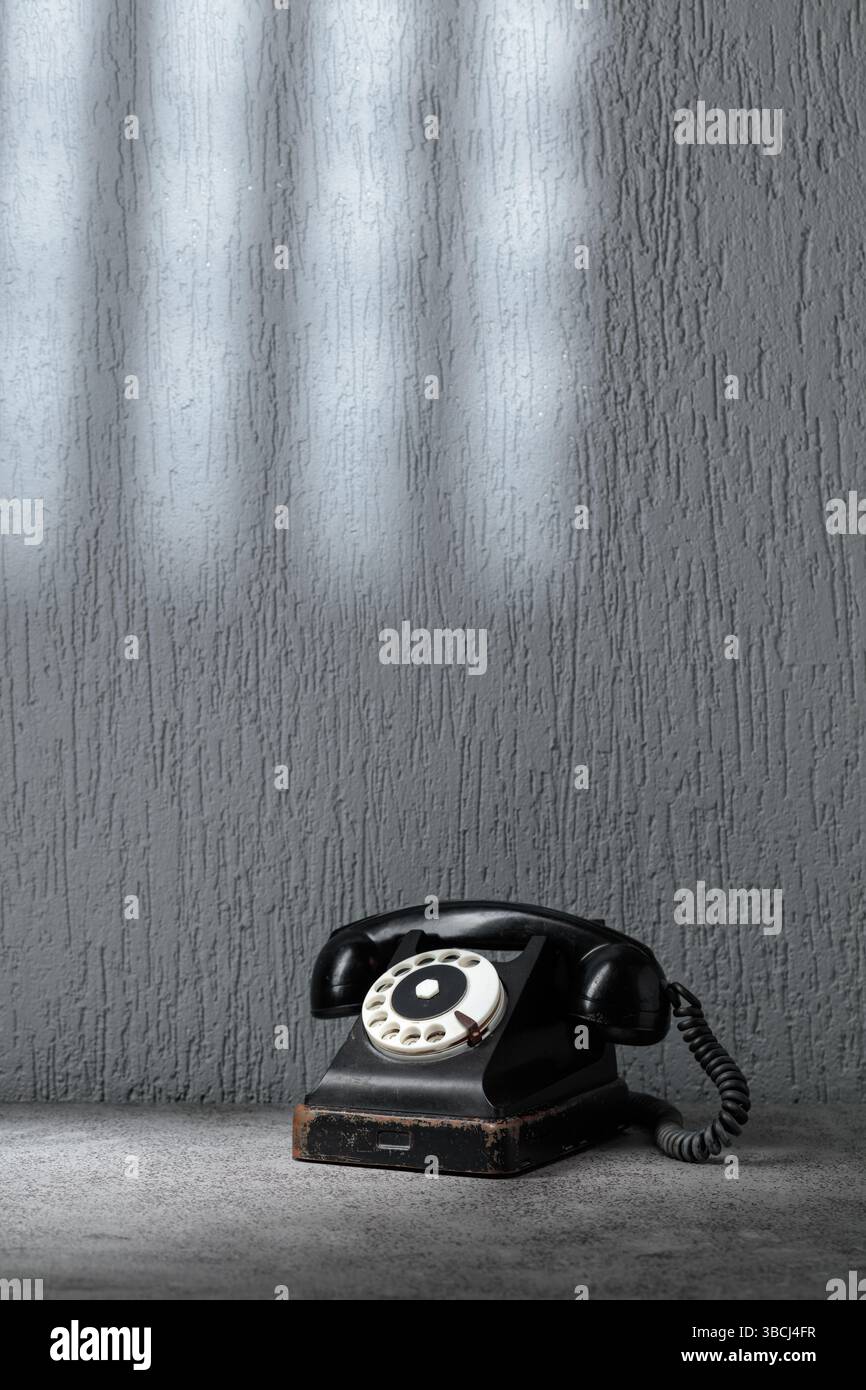 Vintage black telephone with rotary dial on gray stone table. A beam of ...