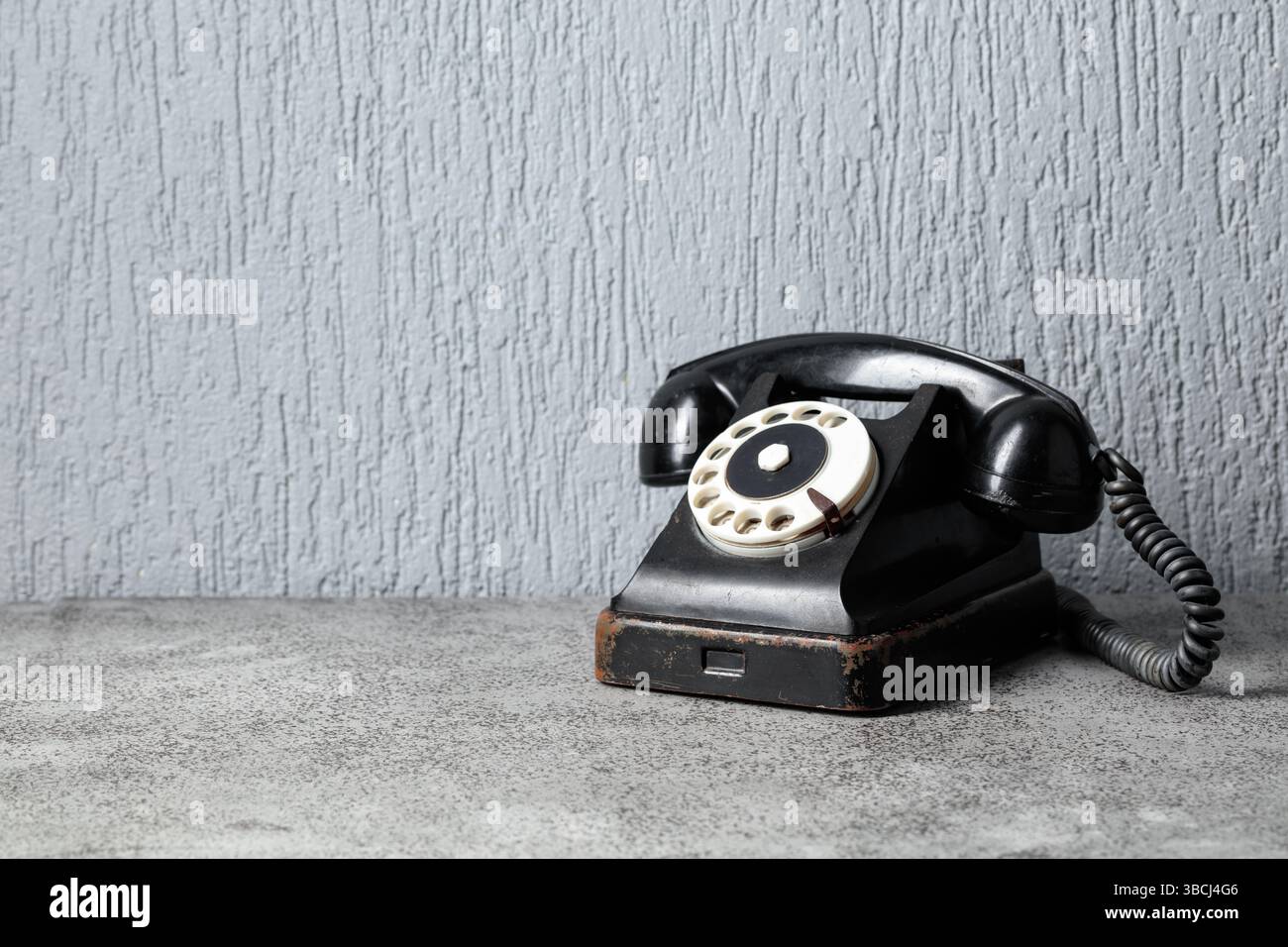 Vintage black phone with rotary dial on a grey stone table. Copy space ...