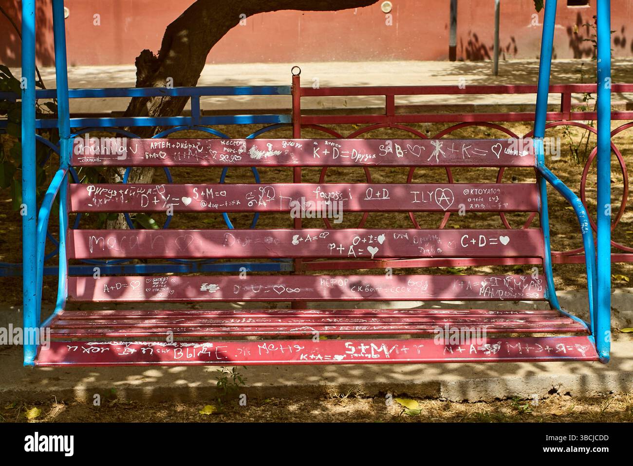 An old red swing with a blue frame and scratched messages holds ...