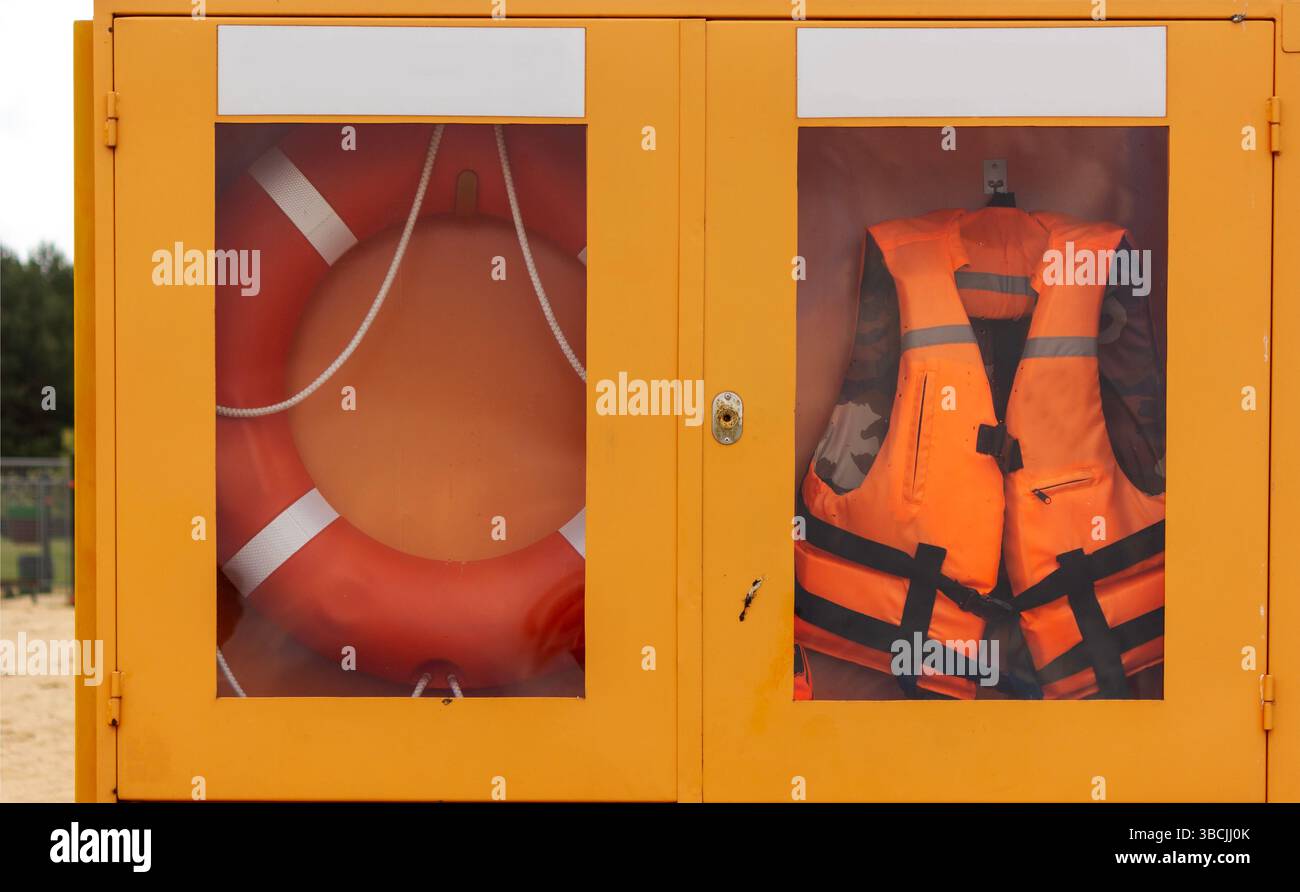 There are life-saving equipment, a lifebuoy and orange life jackets hanging in a wooden cabinet ...