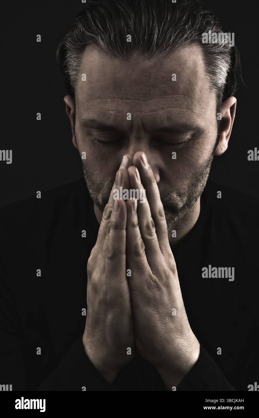 Portrait of sad man praying on a dark background Stock Photo - Alamy