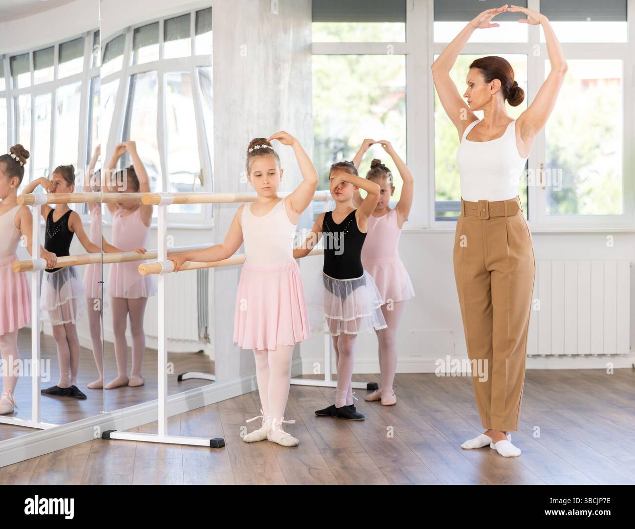 Girl students of choreographic school look at woman teacher and repeat ...