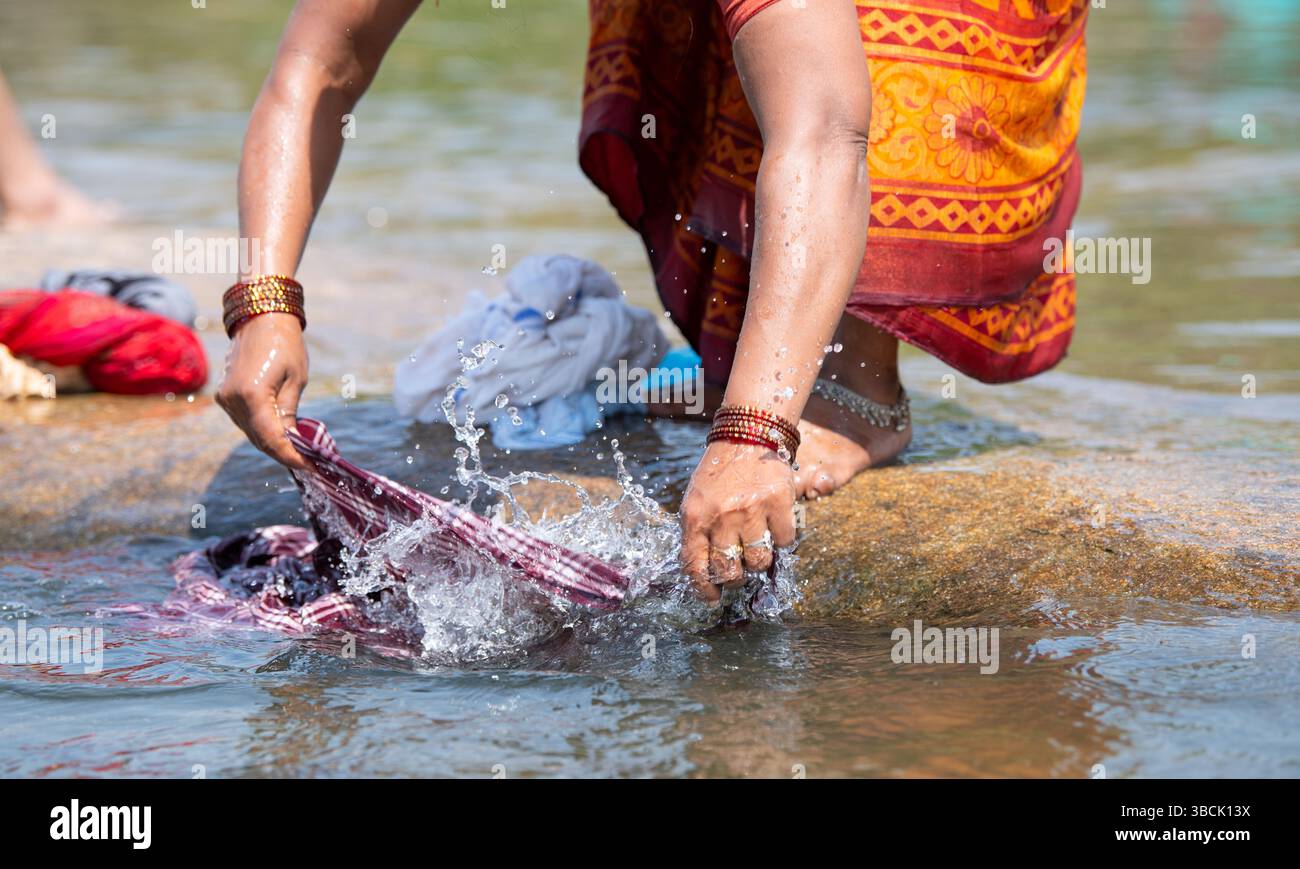 Indian woman washing clothes at Tungabhadra river, Hampi, colorful fabrics, traditional bangles ...