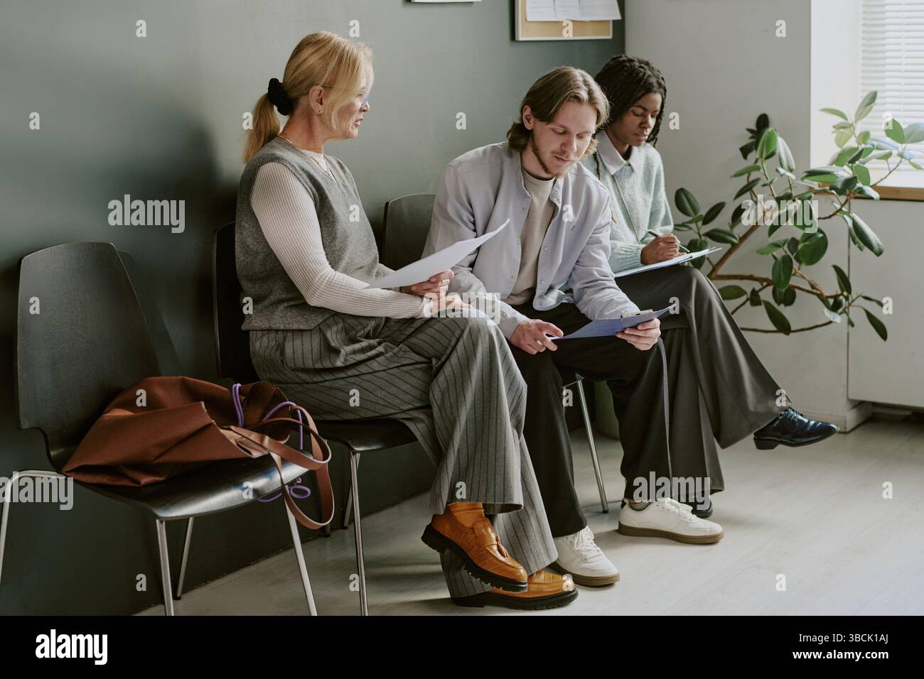 Three biracial people sitting on bench and communicating with each ...