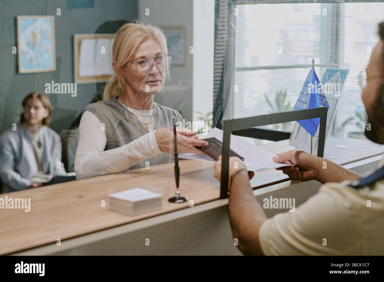 Senior woman handing papers to official at government office counter ...
