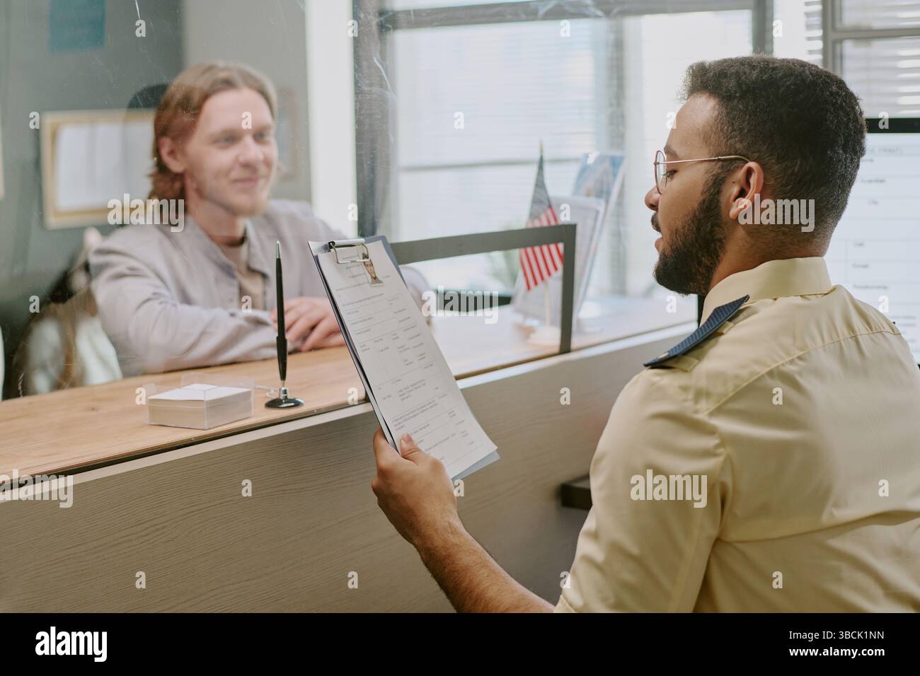 Two men engaging in conversation at reception desk, one holding ...