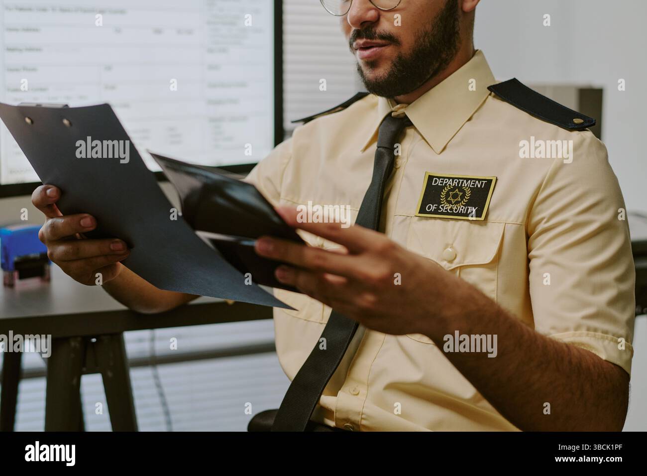 Security guard sitting at desk in office holding documents and wearing ...