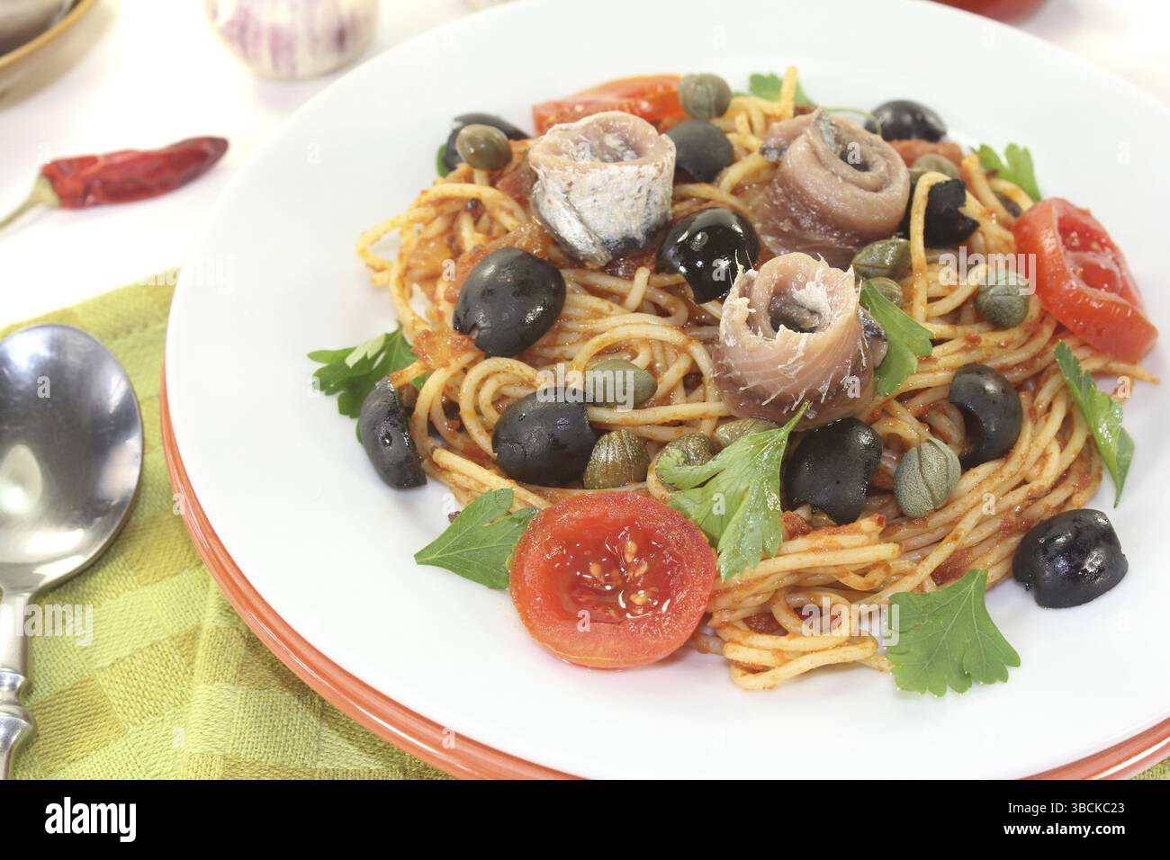 Spaghetti alla puttanesca with anchovies on a light-coloured background ...