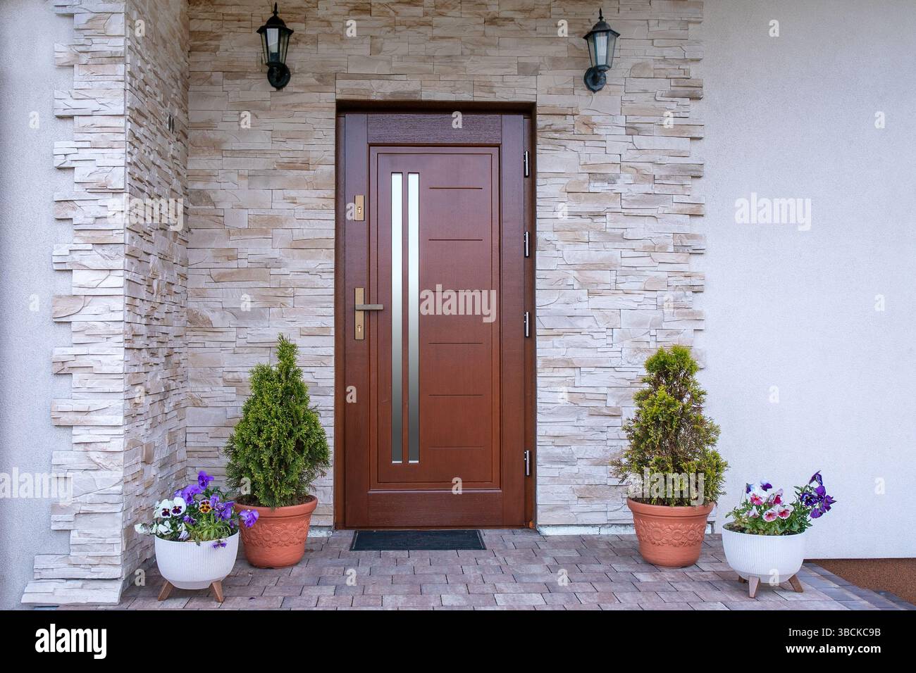 A front door detail with a stone accent wall, a brown door, covered ...