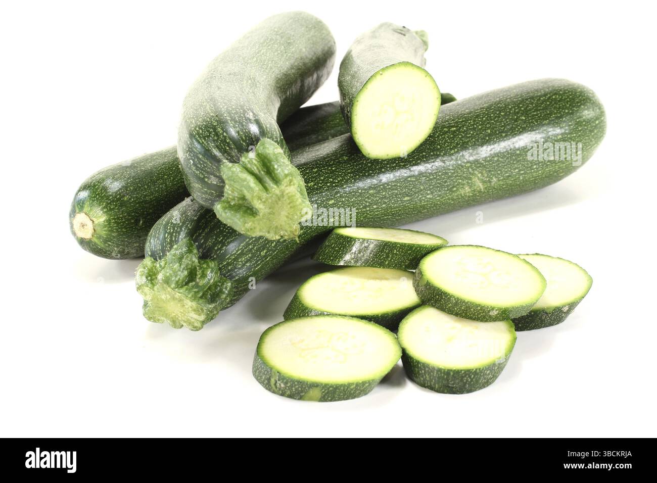 Fresh sliced and whole courgettes against a light-coloured background ...