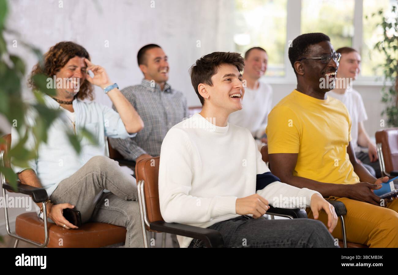 Cheerful guy listening to presentation with group in conference hall ...