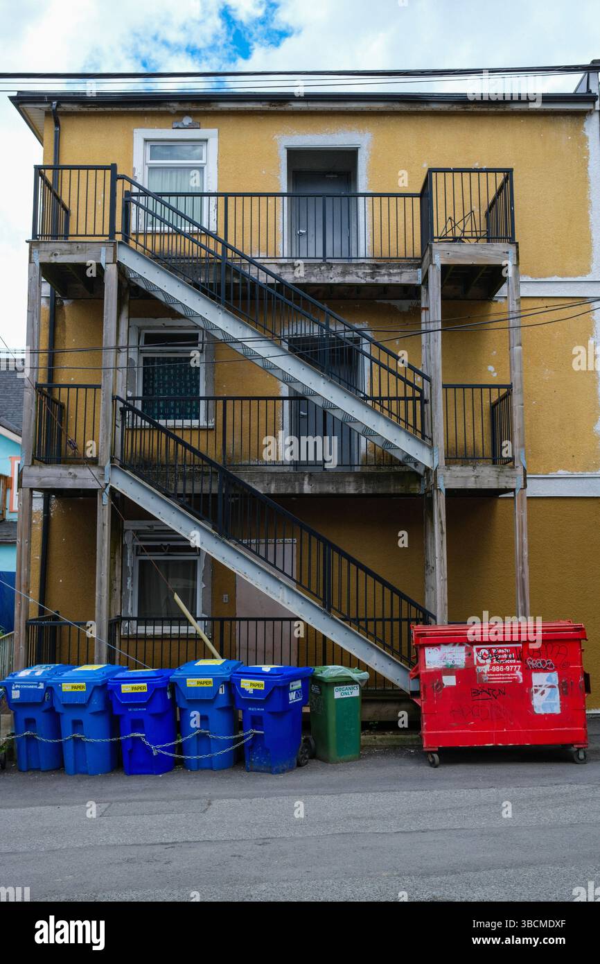 An alley behind an older apartment with garbage & recycling bins at the ...