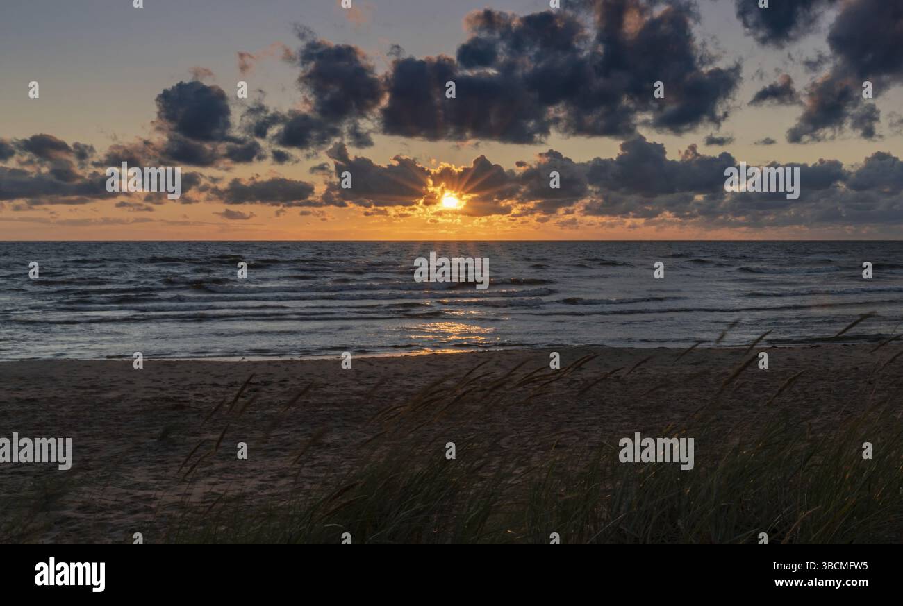 A colorful beach sunset with the sun dropping into the ocean under an ...