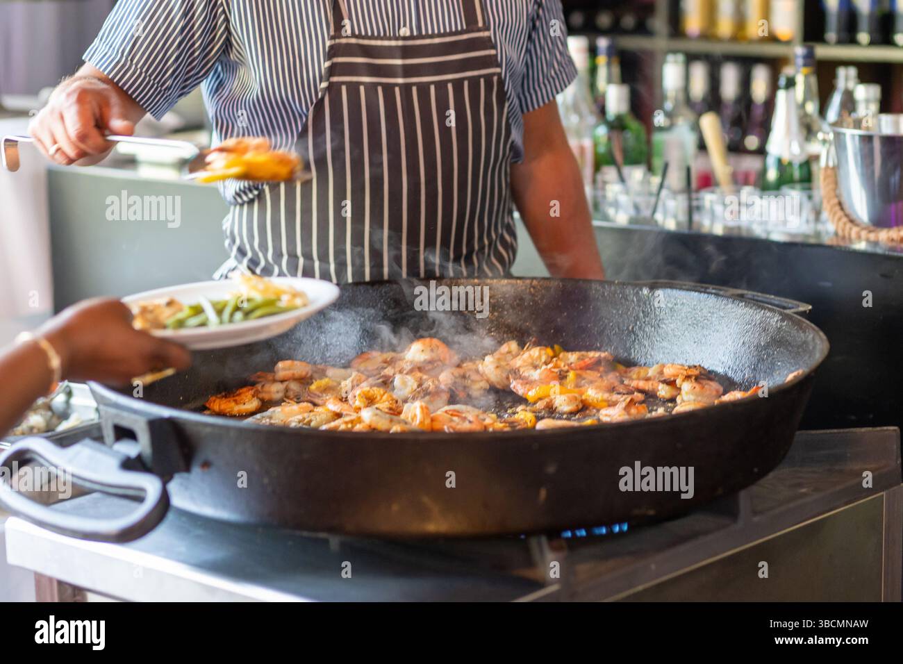A chef stirs a massive skillet filled with shrimp and vegetables ...