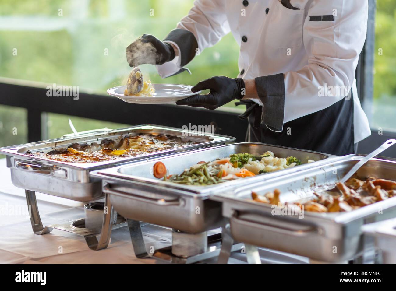 A caterer in a professional outfit serves a plate of food from a buffet ...