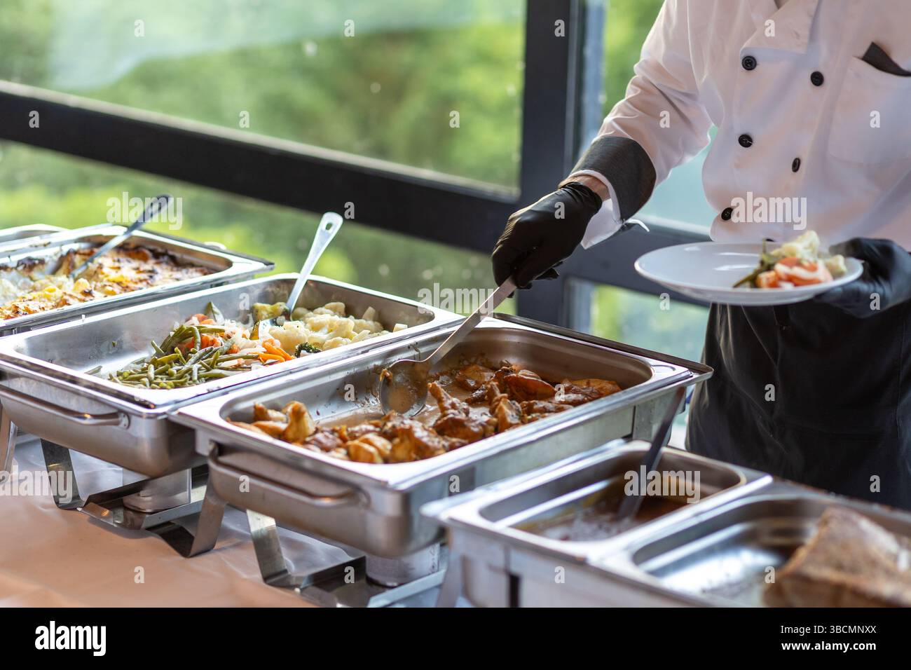 A chef serves food from a buffet setup at a formal event. The trays ...