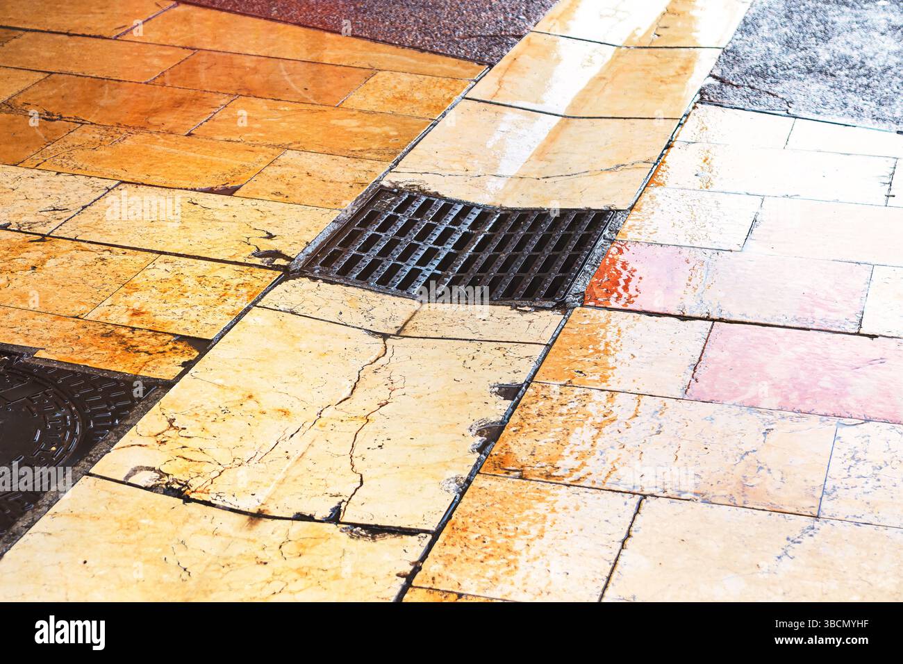 Tiled walkway with drainage grate and manhole cover. Tiles are wet ...