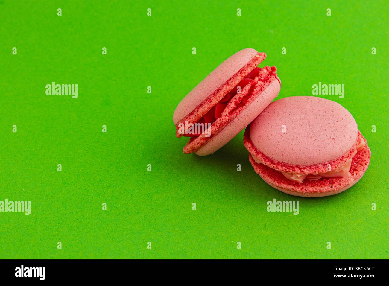 Pink macarons rest slightly tilted on a bright green background ...