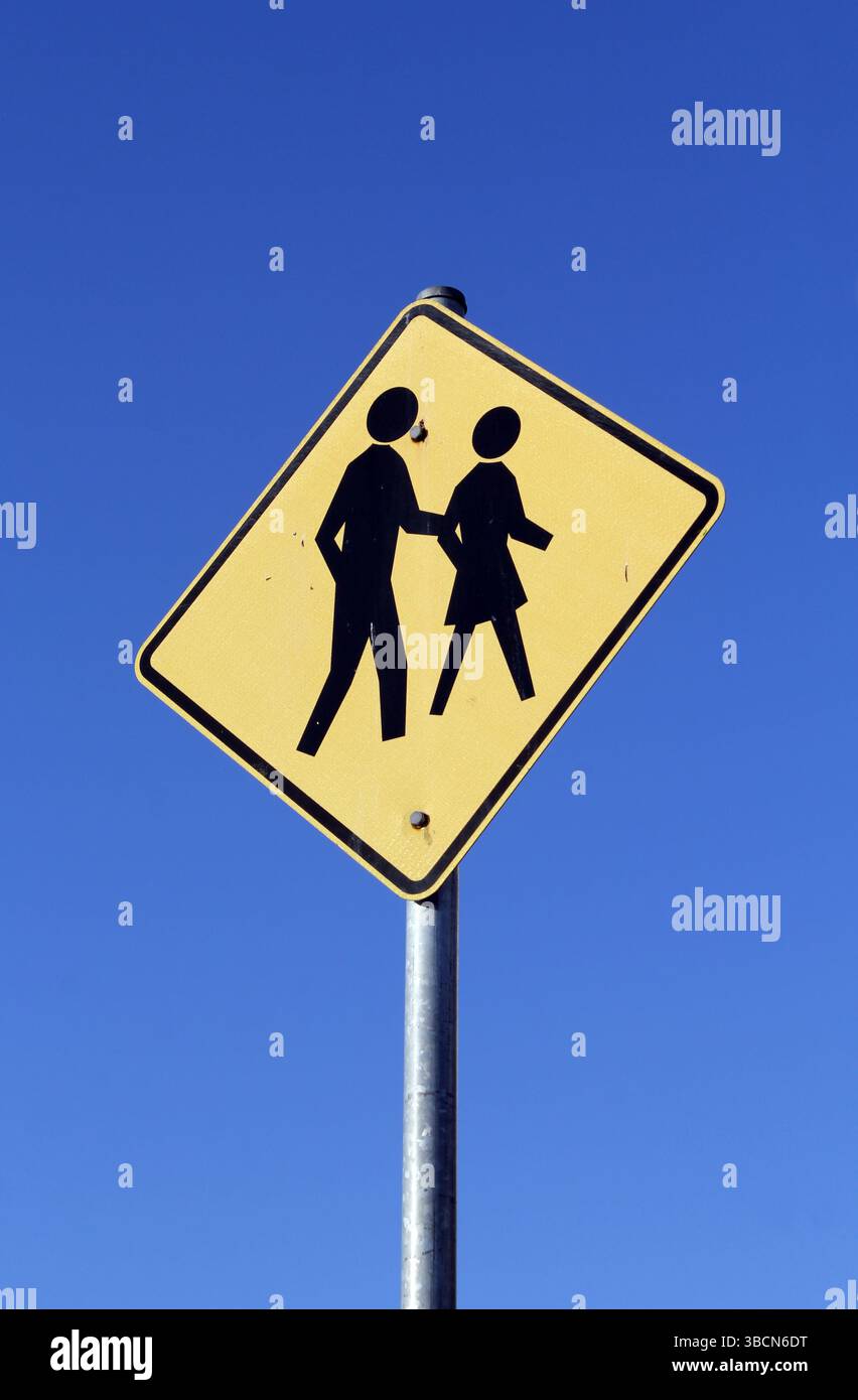 Yellow pedestrian crossing school zone road sign against a clear blue ...