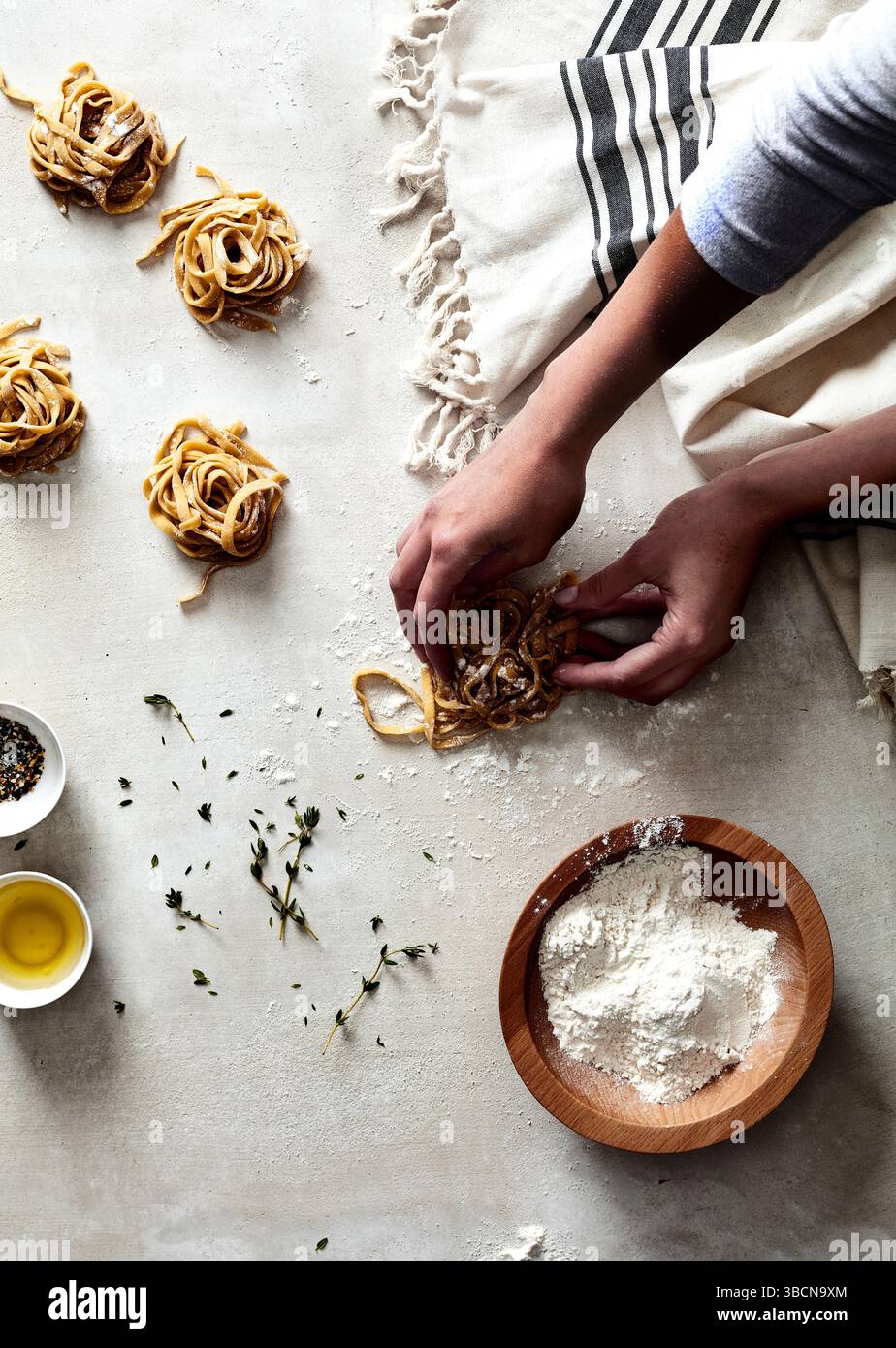 Hands shaping fresh pasta nests on floured surface with herbs Stock ...