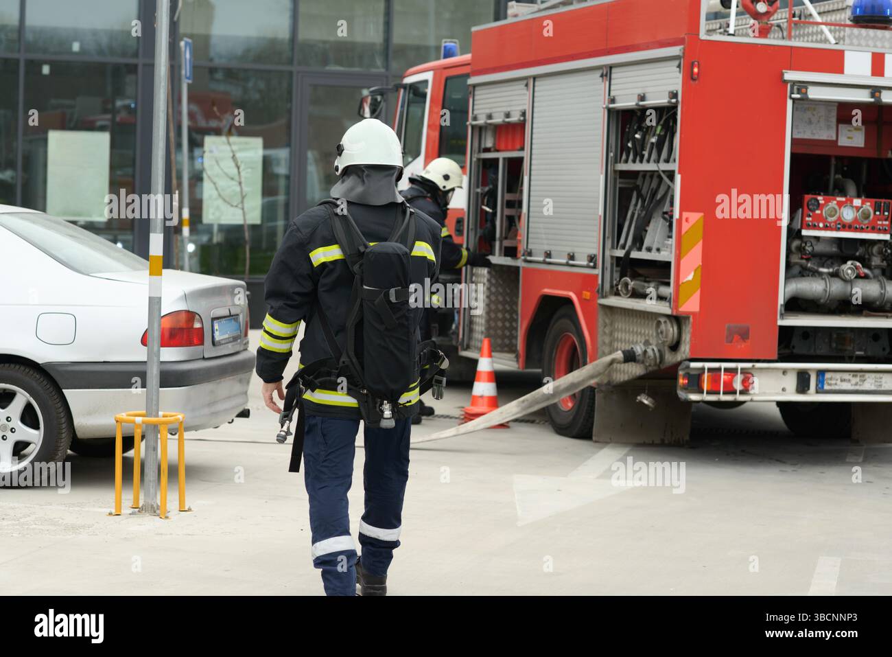 A firefighter in full protective turnout gear walks toward a red fire ...